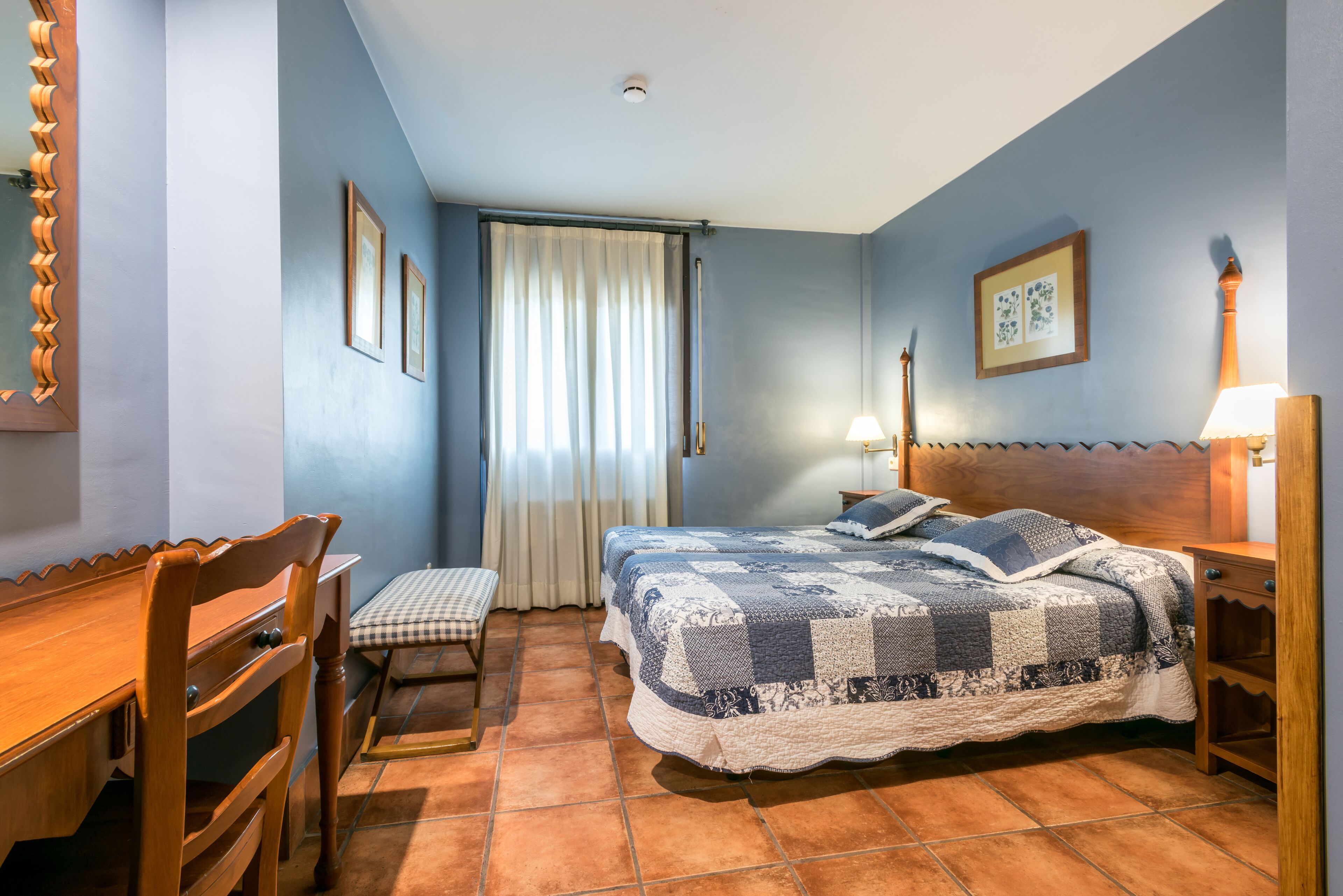 Quarto com cama, escrivaninha, cadeira, mesa de cabeceira e abajur.