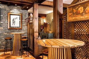 Um interior rústico com uma mesa de madeira e banquetas, uma parede de pedra com um quadro emoldurado e um divisório de madeira treliçada.
