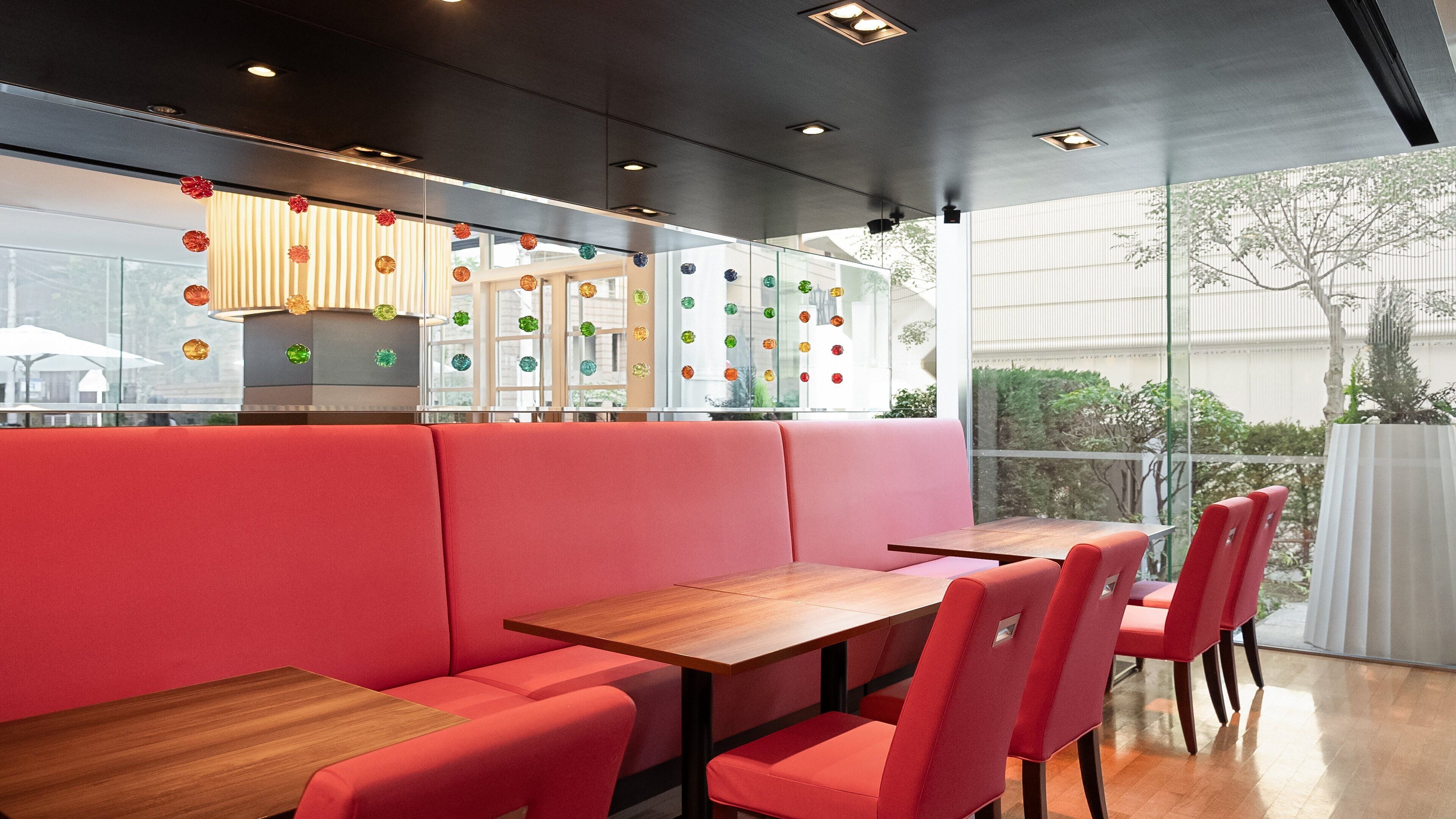 Um restaurante moderno com assentos vermelhos, mesas de madeira e uma parede decorativa com ornamentos de vidro coloridos.