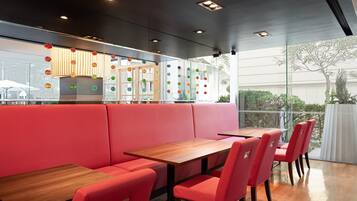 Um restaurante moderno com assentos vermelhos, mesas de madeira e uma parede decorativa com ornamentos de vidro coloridos.