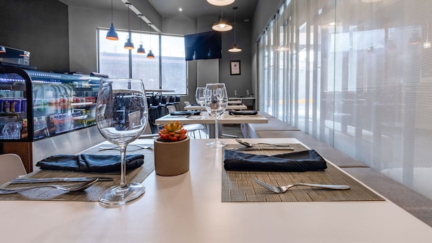 Um restaurante moderno com interior que apresenta uma mesa de jantar comprida, várias cadeiras e um bar com balcão refrigerado.