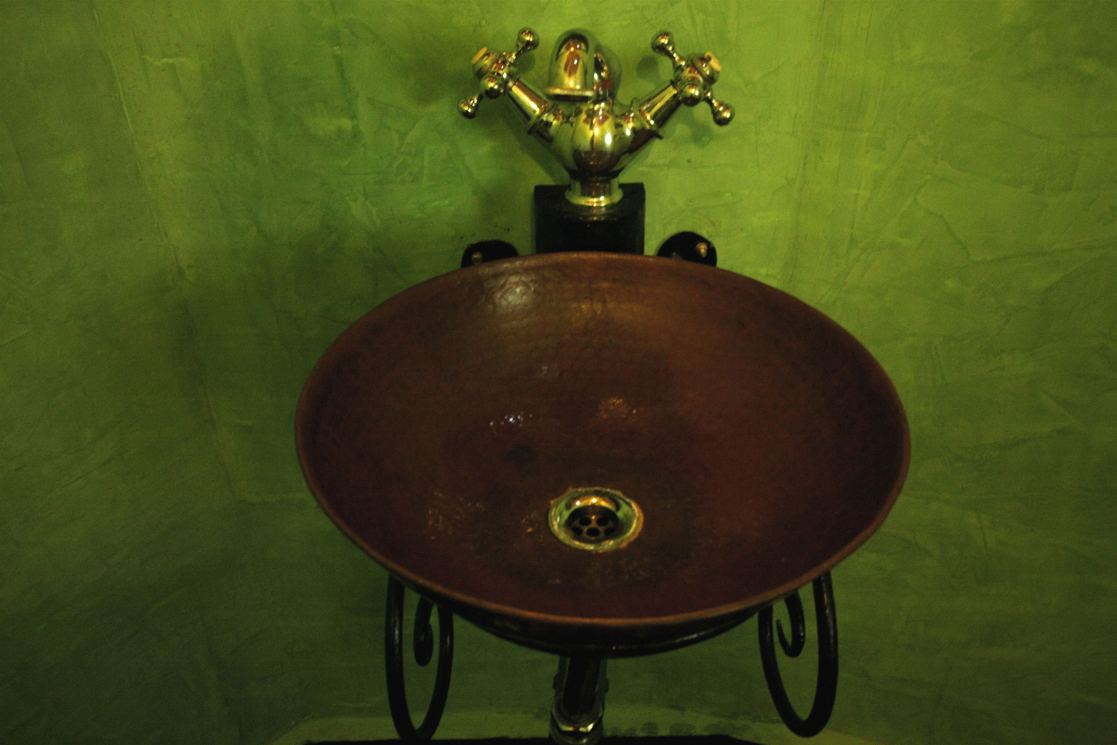 Uma pia de estilo antigo com torneira de latão montada em um pedestal preto, em frente a uma parede verde.