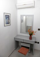 Casa de banho com toucador branco, espelho, quadro emoldurado, um vaso com flores e unidade de ar condicionado.