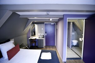 Quarto de hotel com cama, escrivaninha e banheiro.