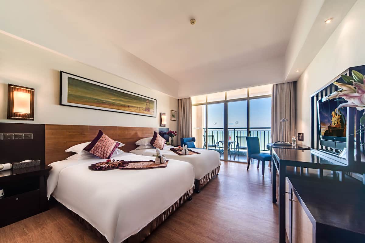 Quarto de hotel com duas camas, uma janela grande, varanda e área de refeições.