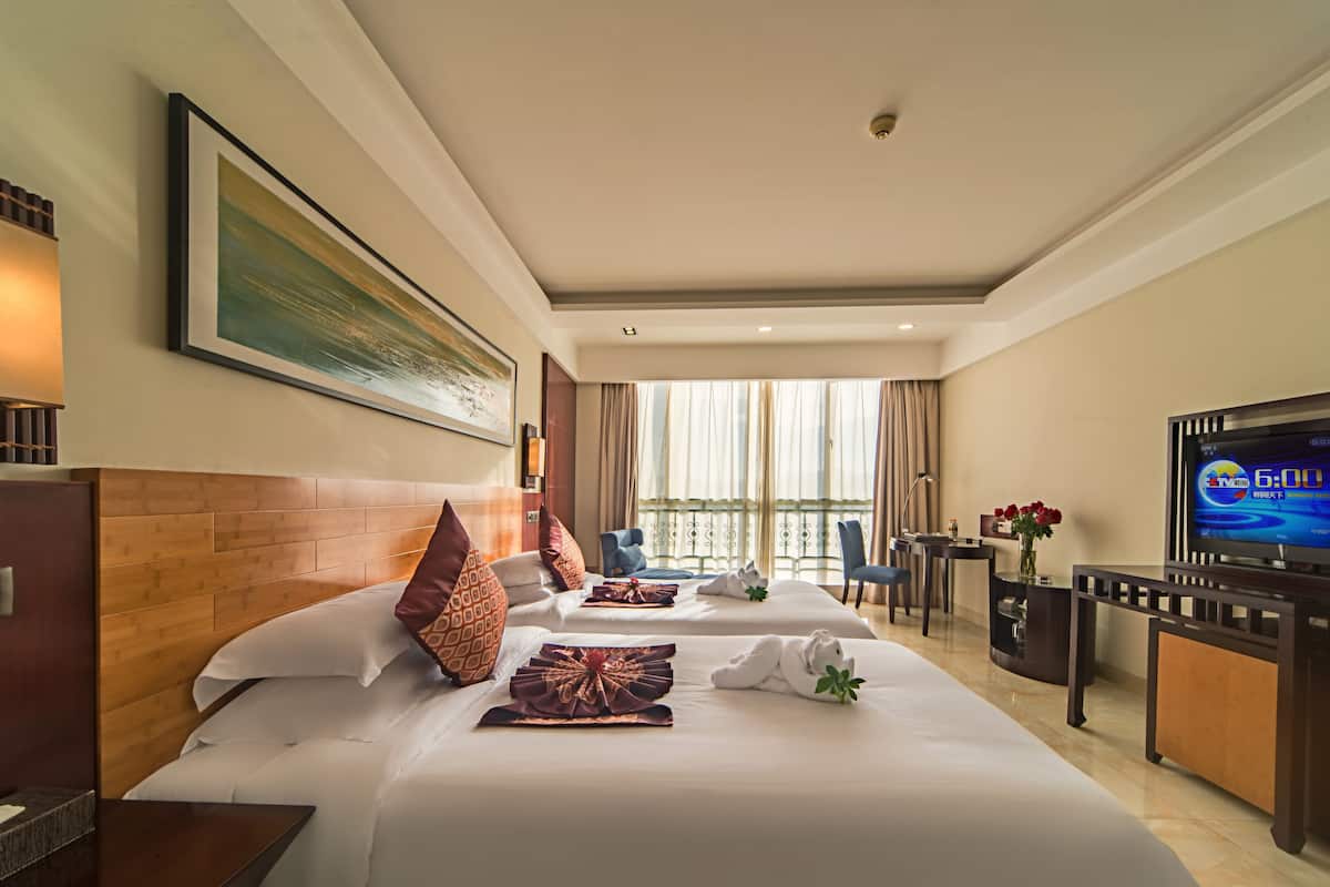 Quarto de hotel com duas camas, televisão, escrivaninha e janela com cortinas.