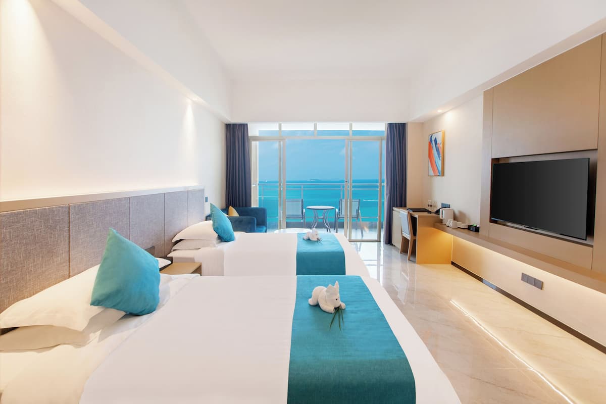 Quarto de hotel com duas camas, televisão e vista para o mar.