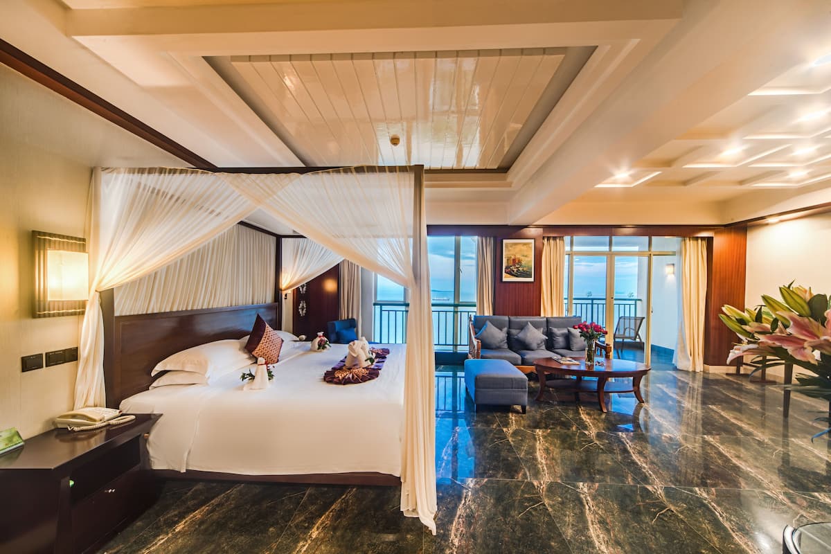 Quarto de hotel espaçoso com cama grande, varanda, área de estar e vista para o mar.