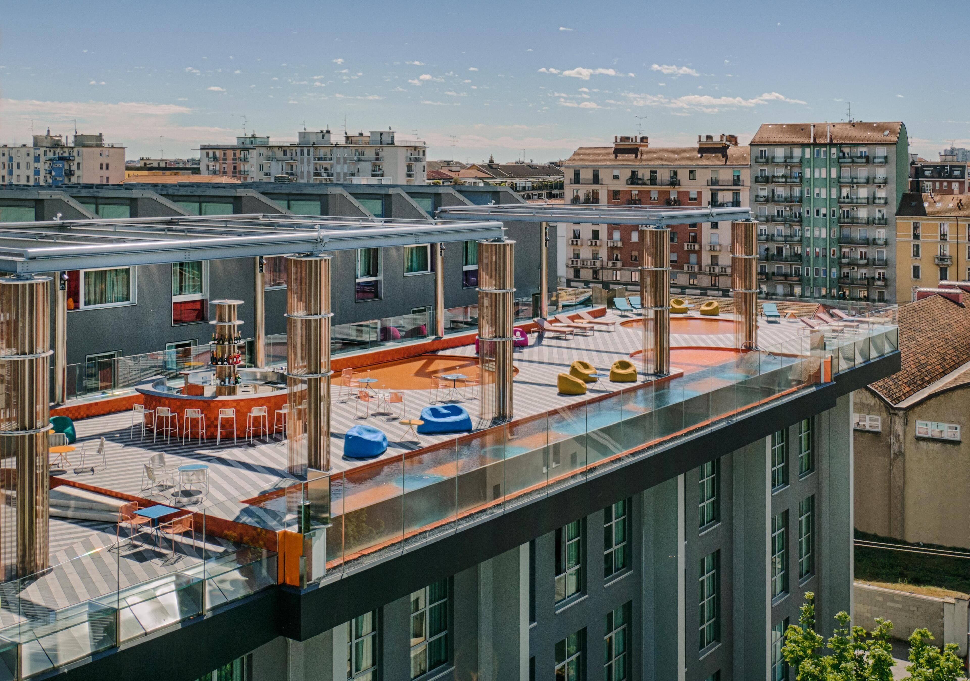 Um terraço no topo com áreas de estar, um bar e guarda-corpo de vidro.