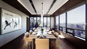 Uma sala de conferência moderna com uma mesa grande preparada para uma reunião, janelas amplas com vista para a cidade e um detalhe decorativo na parede.