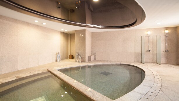 Piscina interior moderna com design curvo, rodeada por paredes bege e equipada com várias luminárias.