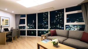 Uma sala de estar moderna com uma janela grande, um sofá, uma mesa de centro, uma escrivaninha com um laptop e um quadro na parede.