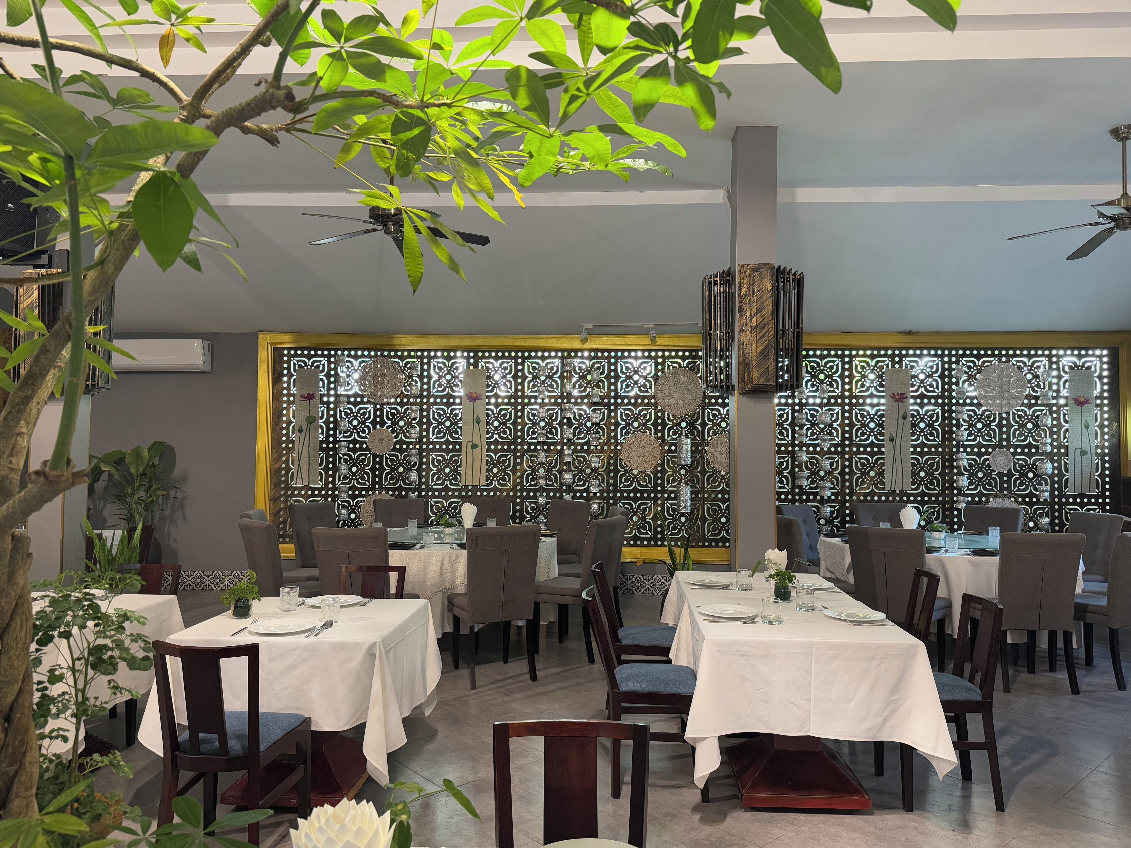 Restaurante com várias mesas, cadeiras e uma parede decorativa com padrões iluminados.