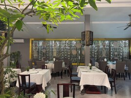 Restaurante com várias mesas, cadeiras e uma parede decorativa com padrões iluminados.