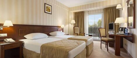 Quarto de hotel com duas camas, uma escrivaninha, uma cadeira, telefone e janela com cortinas.