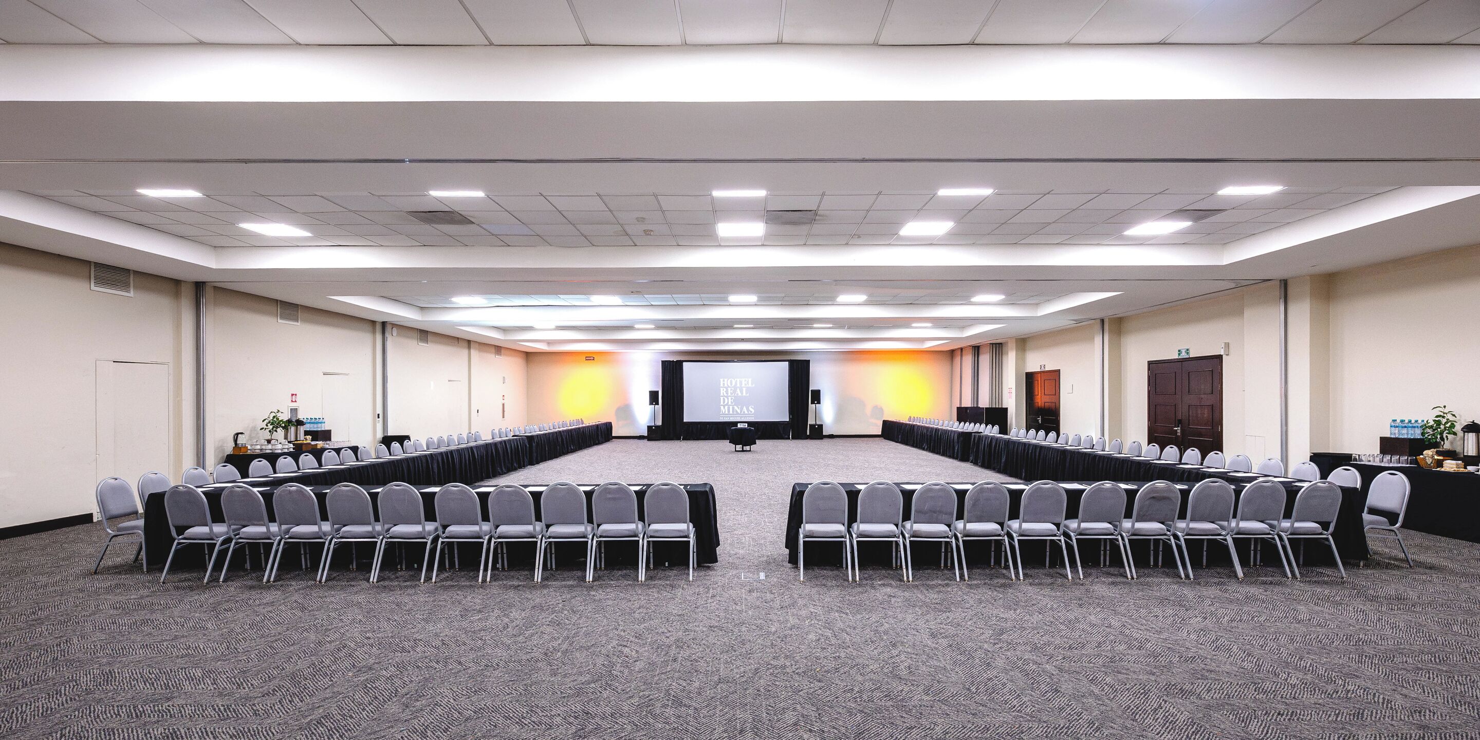 Uma sala de conferências com fileiras de cadeiras, uma tela de projetor e um palco.