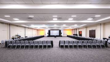 Uma sala de conferências com fileiras de cadeiras, uma tela de projetor e um palco.