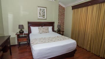 Uma cama bem arrumada com cabeceira de madeira, uma mesa de cabeceira com abajur, e uma parede de tijolos ao fundo.