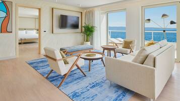 Quarto de hotel moderno com uma cama grande, um sofá, uma mesa de centro e uma varanda vista para o mar.