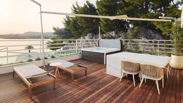 Um deck de madeira com mesa e cadeiras, um sofá e uma banheira de hidromassagem.