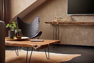 Quarto moderno com mesa de madeira, uma cadeira preta, um vaso de plantas e uma TV de tela plana na parede.
