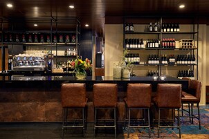 Uma área de bar com balcão, banquetas e prateleiras cheias de garrafas de vinho.