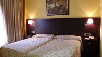 Quarto de hotel com duas camas, um quadro na parede e duas luminárias de cabeceira.
