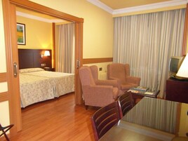 Quarto de hotel com duas camas, uma escrivaninha com cadeira, televisão e janela com cortinas.