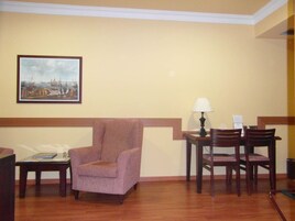 Um quarto com uma cadeira de madeira, uma mesinha com abajur e um quadro pendurado na parede.
