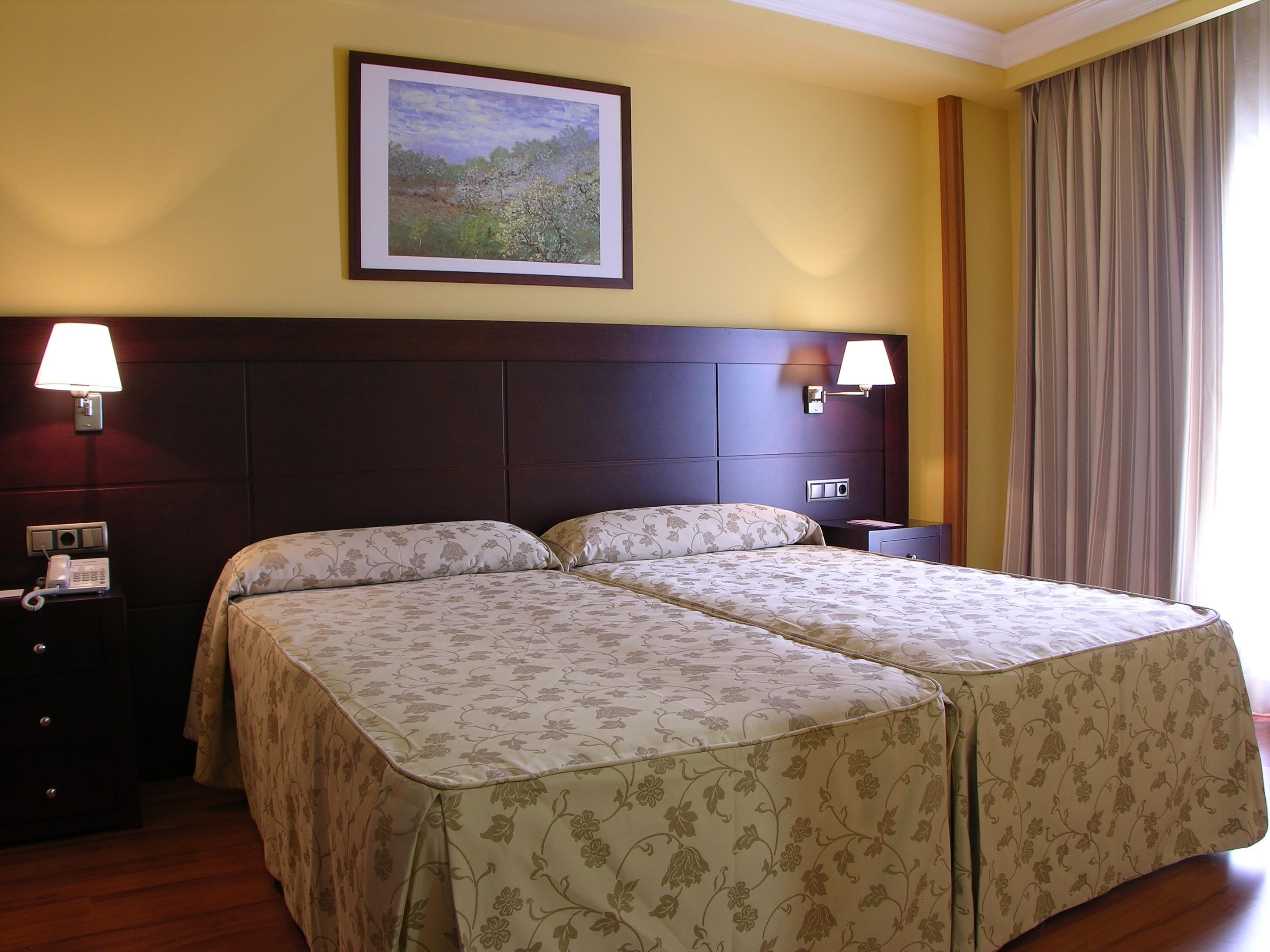 Quarto de hotel com duas camas, um quadro na parede e duas luminárias de cabeceira.