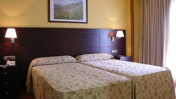 Quarto de hotel com duas camas, um quadro na parede e duas luminárias de cabeceira.