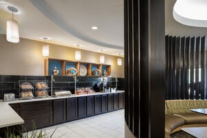 Um lobby de hotel moderno com um balcão de café da manhã, área de estar e uma grande janela.