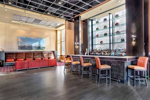 Uma área de bar com um balcão comprido, diversas opções de assento incluindo um sofá e banquetas, e uma janela grande exibindo diversos capacetes esportivos.
