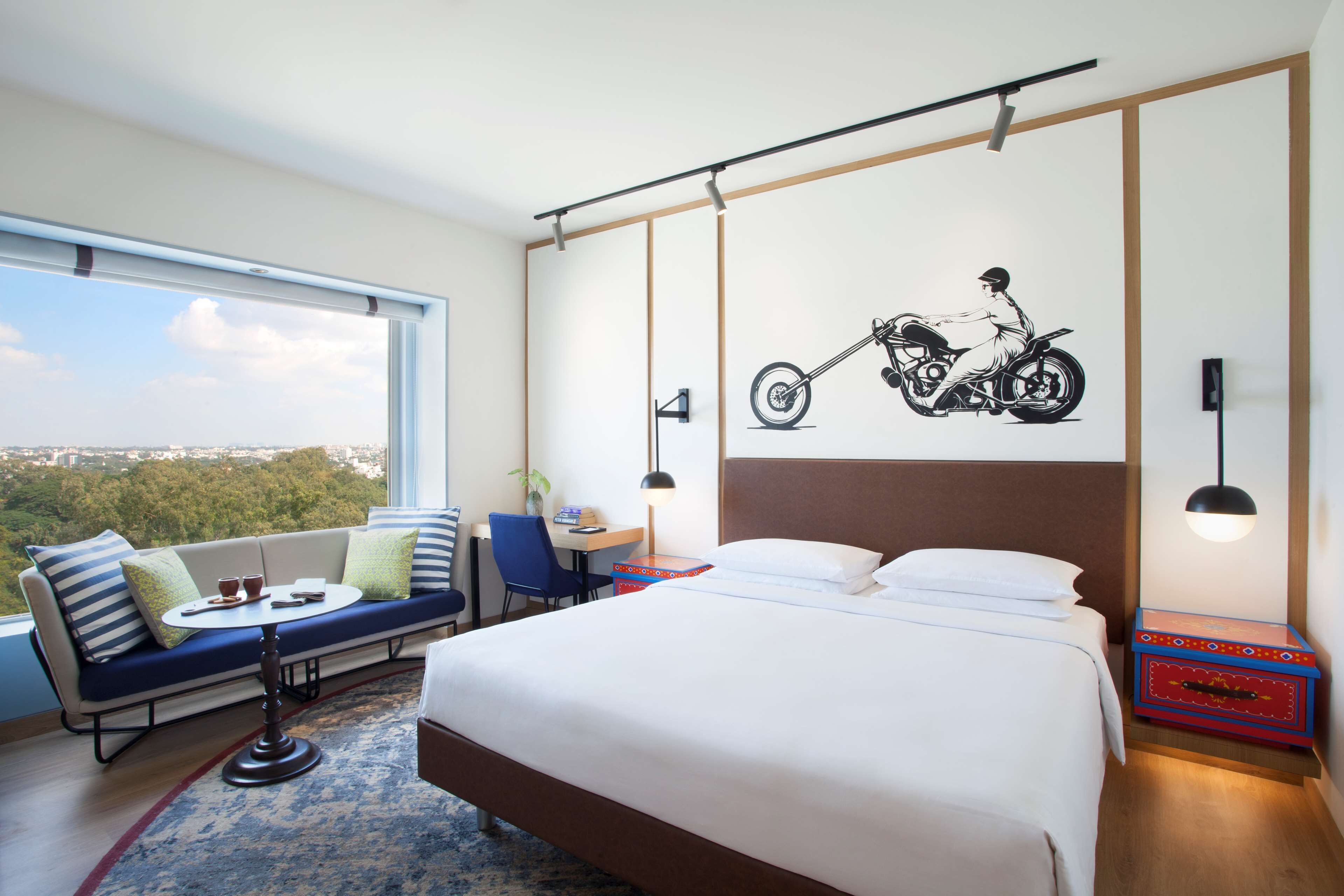 Quarto de hotel com uma cama grande, um sofá, uma escrivaninha e vista para a cidade.
