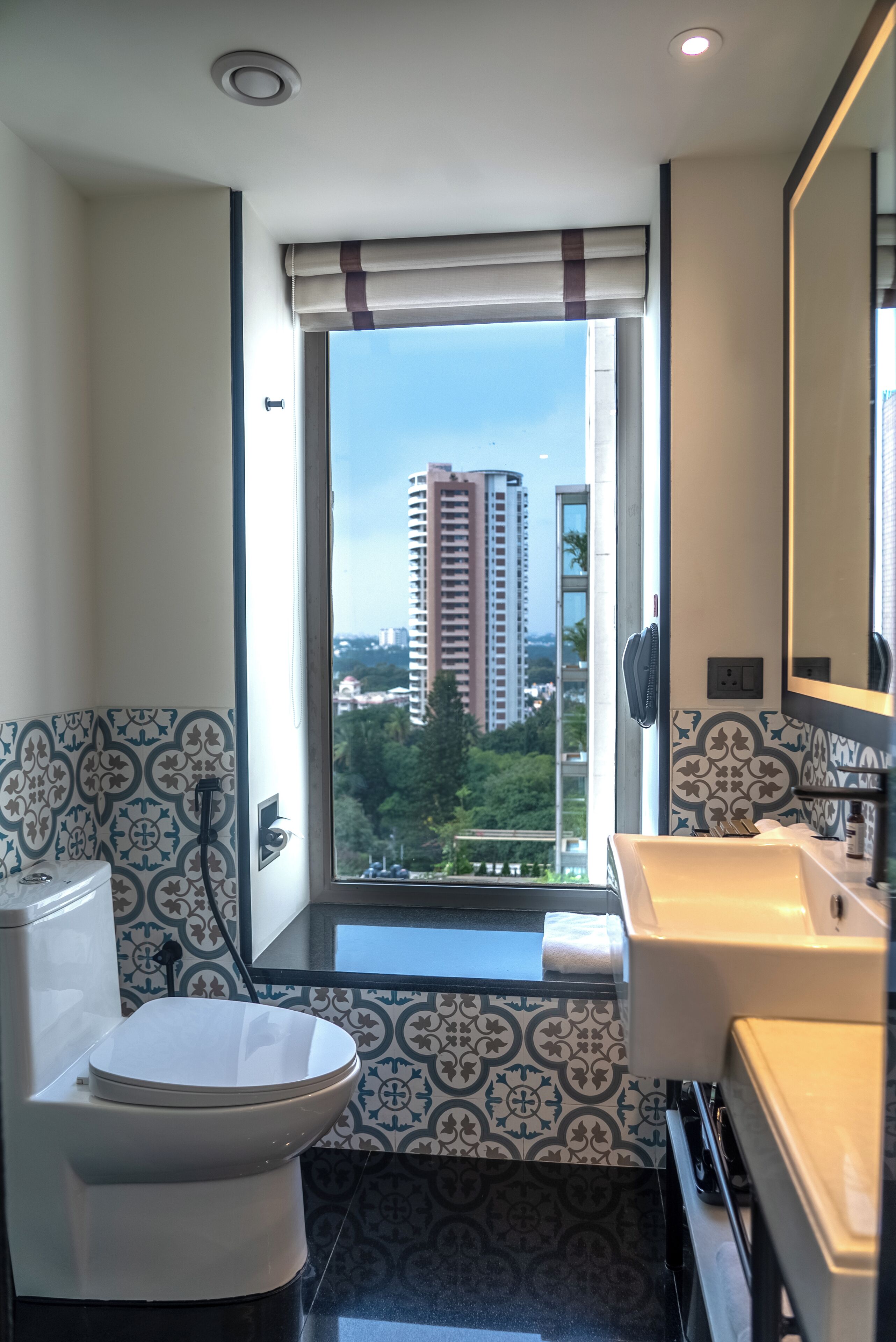 Casa de banho moderna com sanita, lavatório e uma grande janela com vista para a cidade.