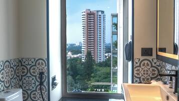 Casa de banho moderna com sanita, lavatório e uma grande janela com vista para a cidade.
