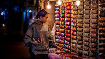 Uma pessoa em uma banca de mercado com pulseiras coloridas e lâmpadas.