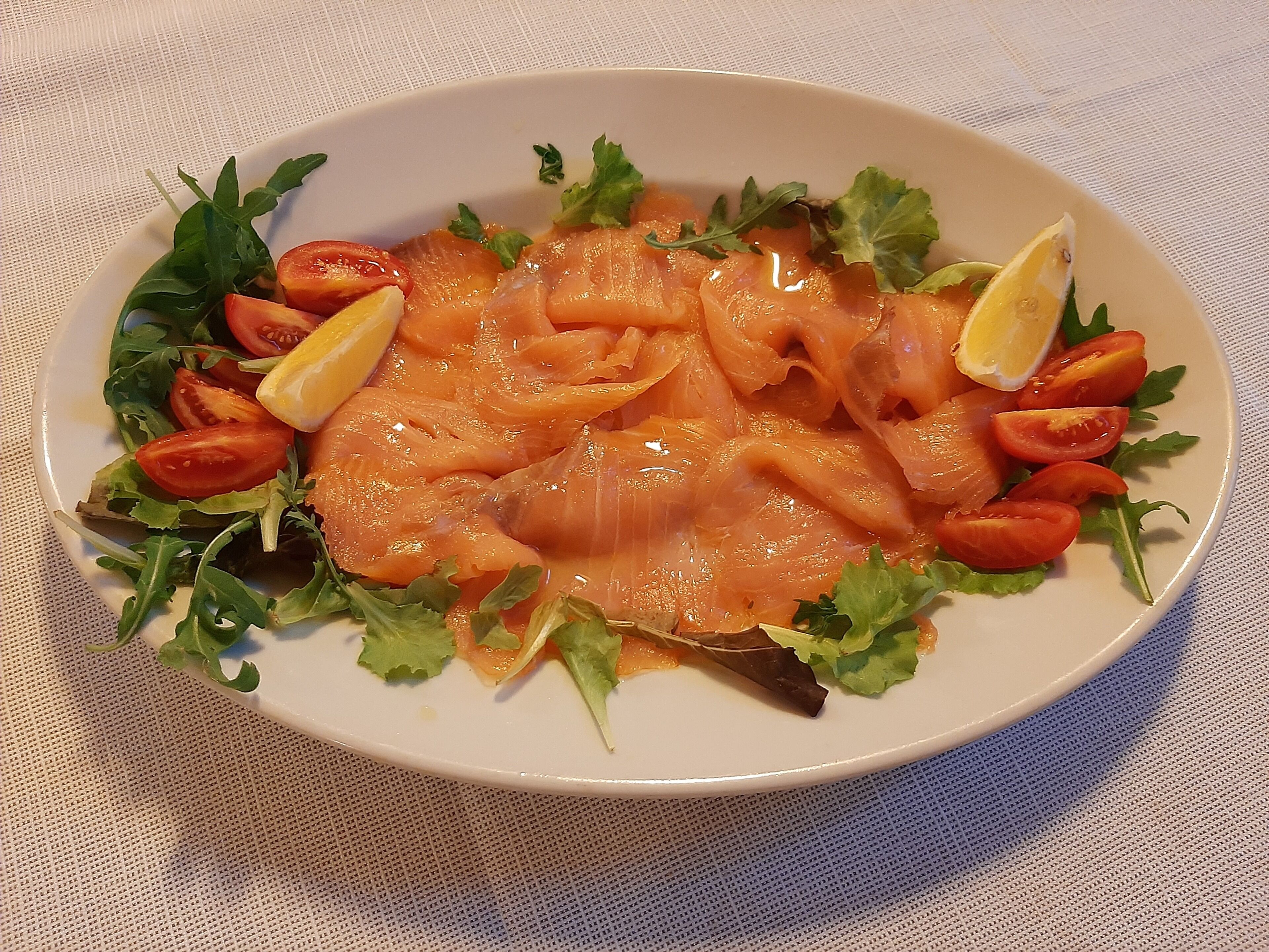 Um prato de salmão com fatias de limão e tomate cereja sobre uma cama de folhas verdes.