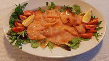 Um prato de salmão com fatias de limão e tomate cereja sobre uma cama de folhas verdes.