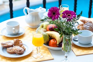 Disposição de café da manhã com croissants, frutas e flores sobre uma mesa perto de uma piscina.