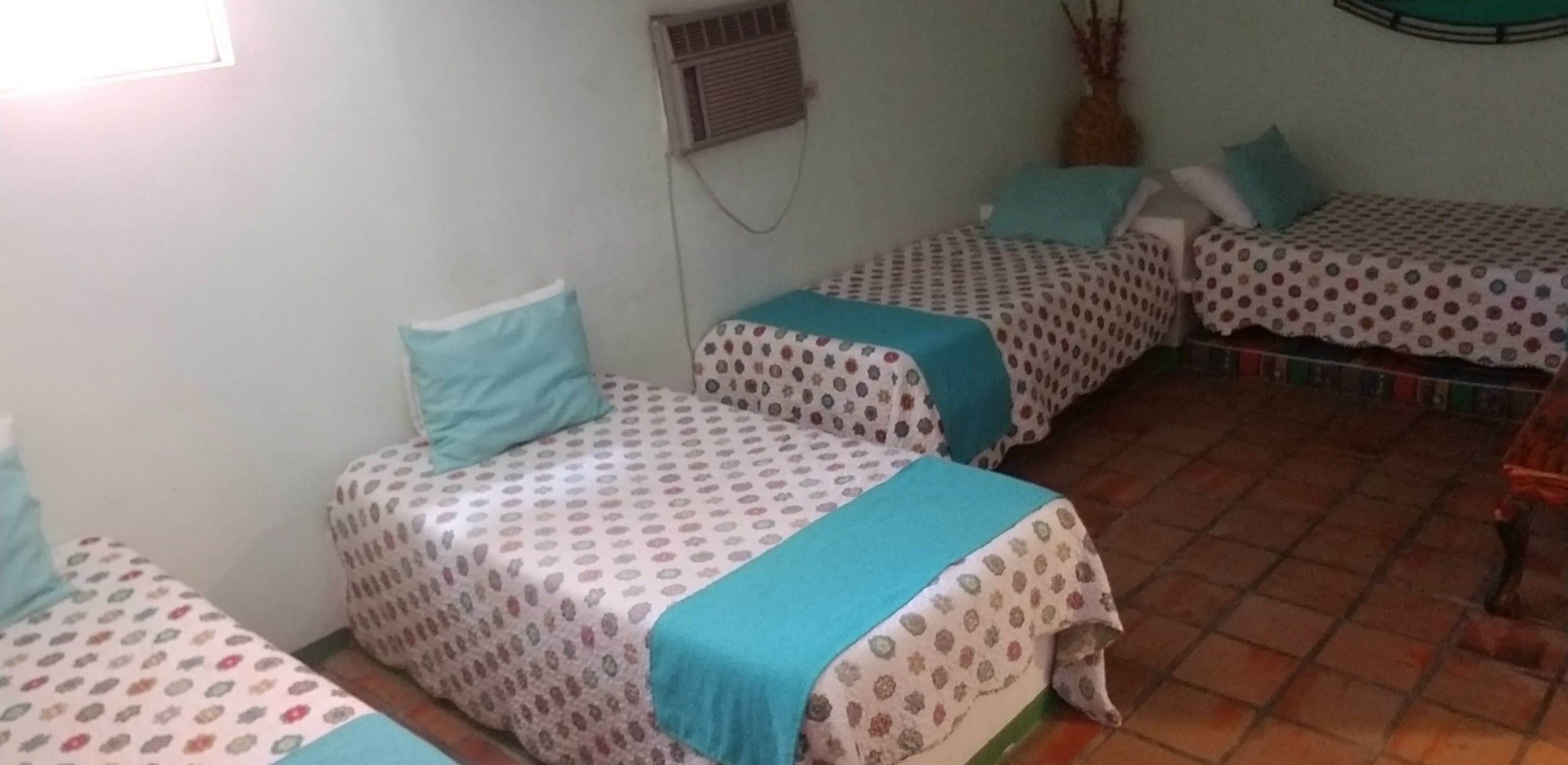 Quarto com três camas, cada uma com roupa de cama estampada e detalhes em azul.