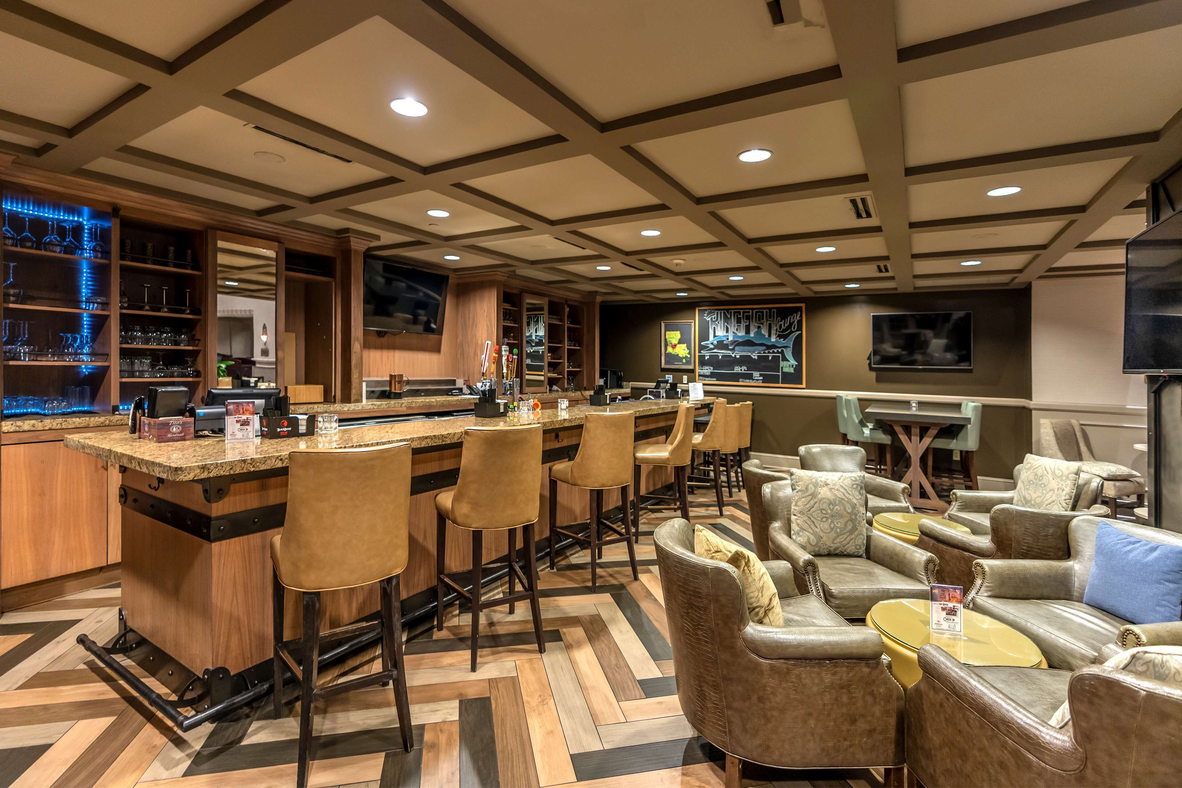 Uma área de bar com balcão, banquetas e um espaço de estar com cadeiras acolchoadas e um sofá.