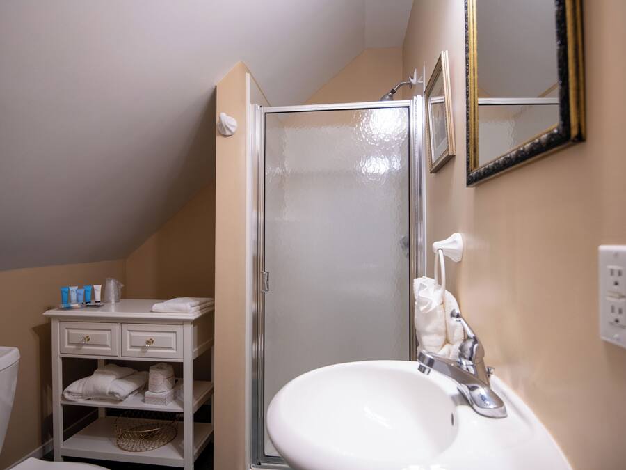 Casa de banho com lavatório branco, cabine de duche em vidro, toucador com espelho e porta-toalhas.