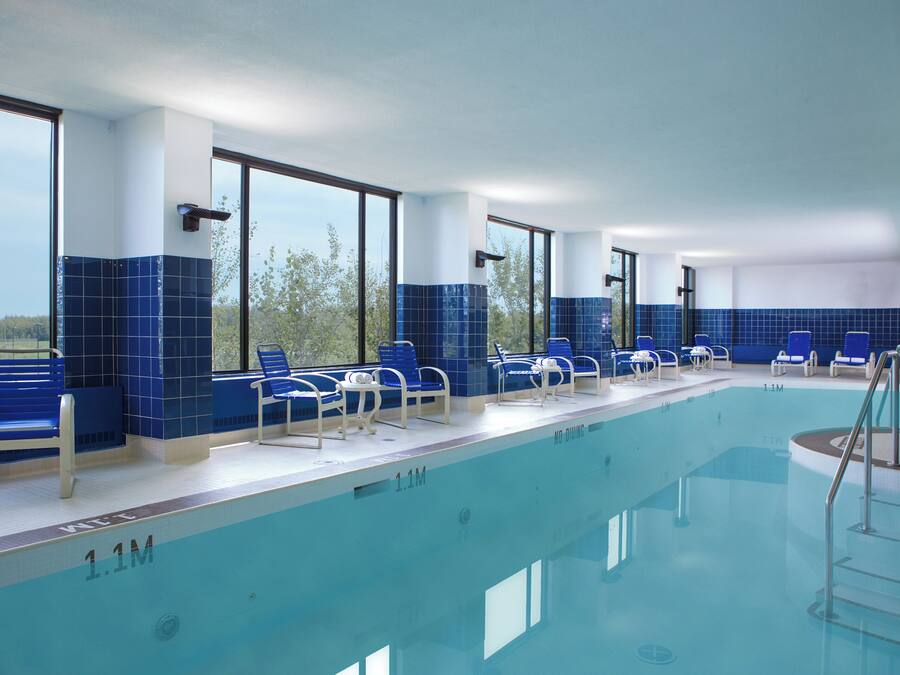 Piscina interior com cadeiras azuis e amplas janelas.