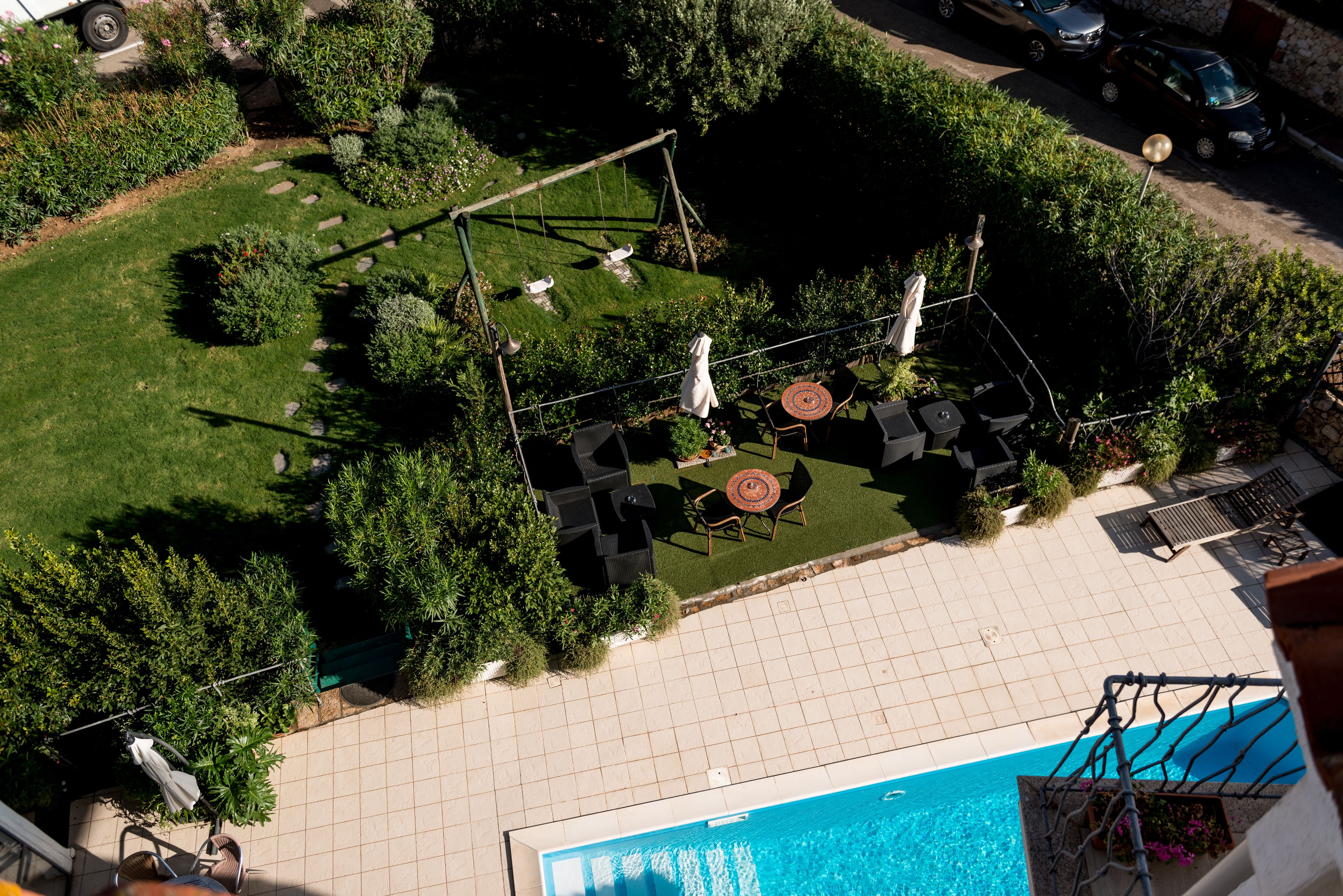 Vista aérea de uma área de piscina no terraço, com balanço, assentos e um pequeno jardim.
