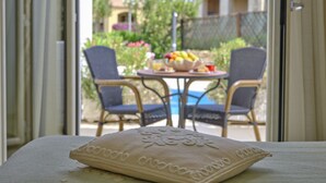 Quarto com cama, travesseiro e vista para um pátio externo com mesa, cadeiras e uma cesta de frutas.