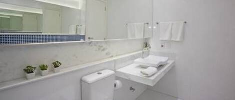 Uma casa de banho moderna com lavatório branco, espelho e sanita. Pequenos vasos com plantas decoram a bancada.