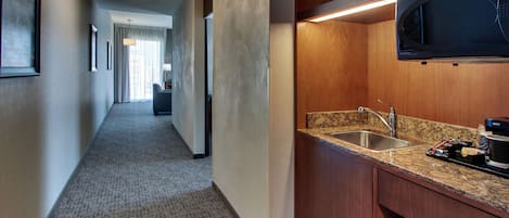 Corredor de hotel com piso carpeteado, parede de madeira, micro-ondas embutido e pia com bancada de granito.