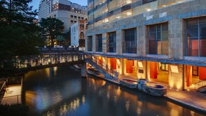 Um hotel com vários andares e fachada de pedra, com uma ponte sobre um canal e áreas de estar ao ar livre.