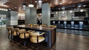 Uma sala de conferências espaçosa com uma mesa comprida e cadeiras de couro, área de bar com banquetas e design de teto moderno.